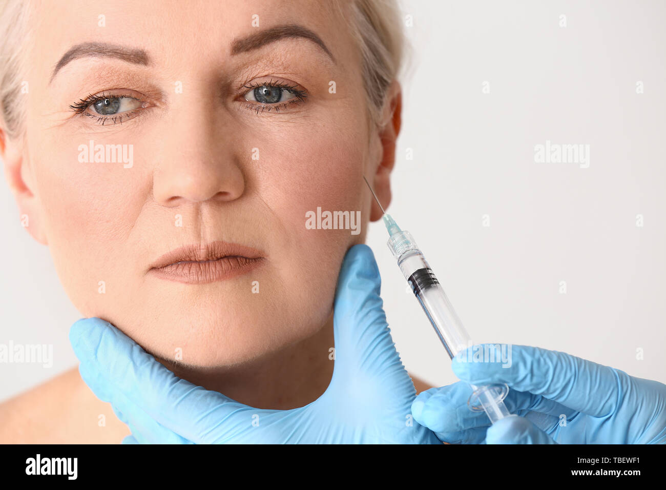 Mature woman receiving injection in face on light background, closeup ...