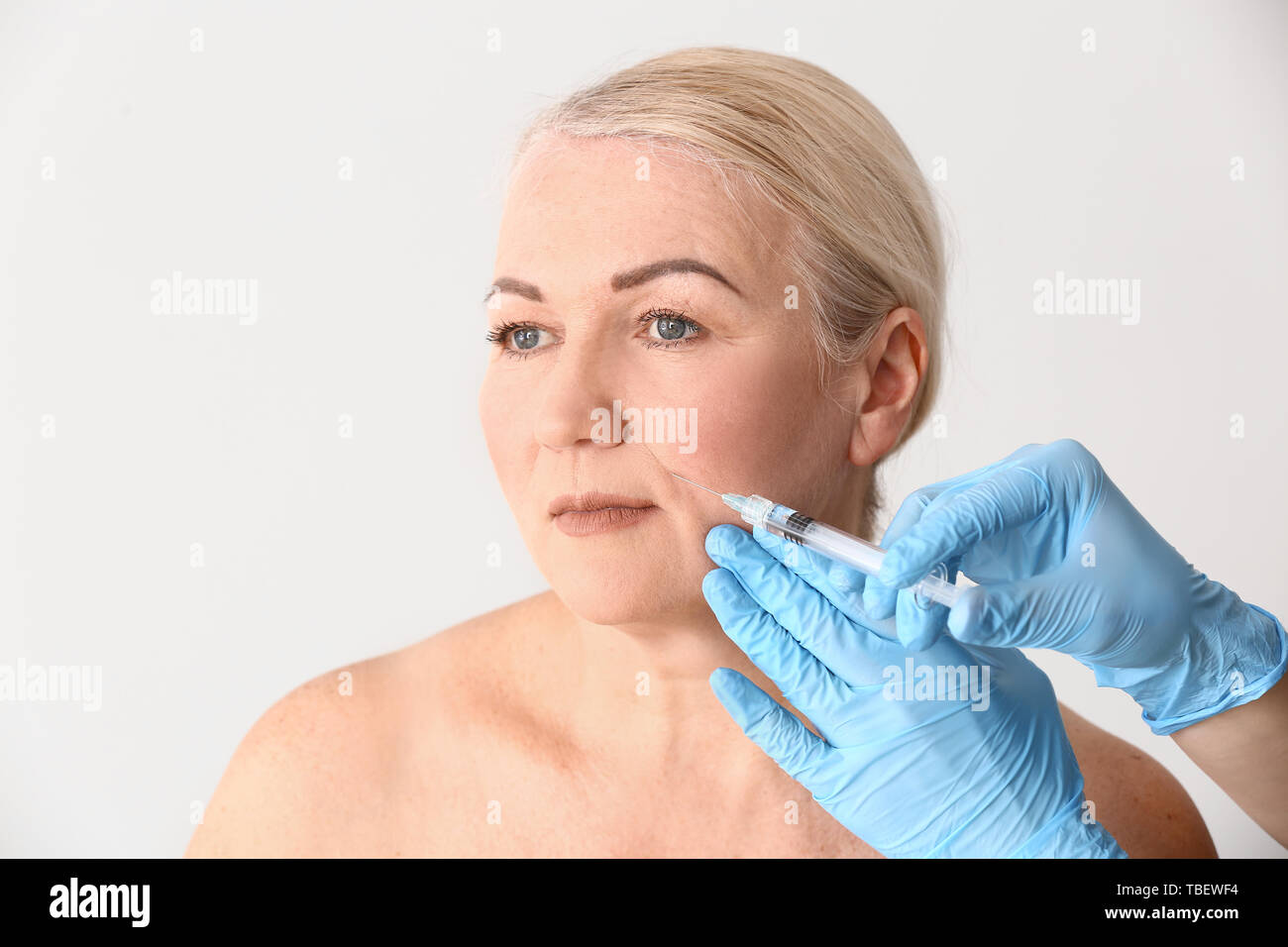 Mature woman receiving injection in face on light background Stock ...
