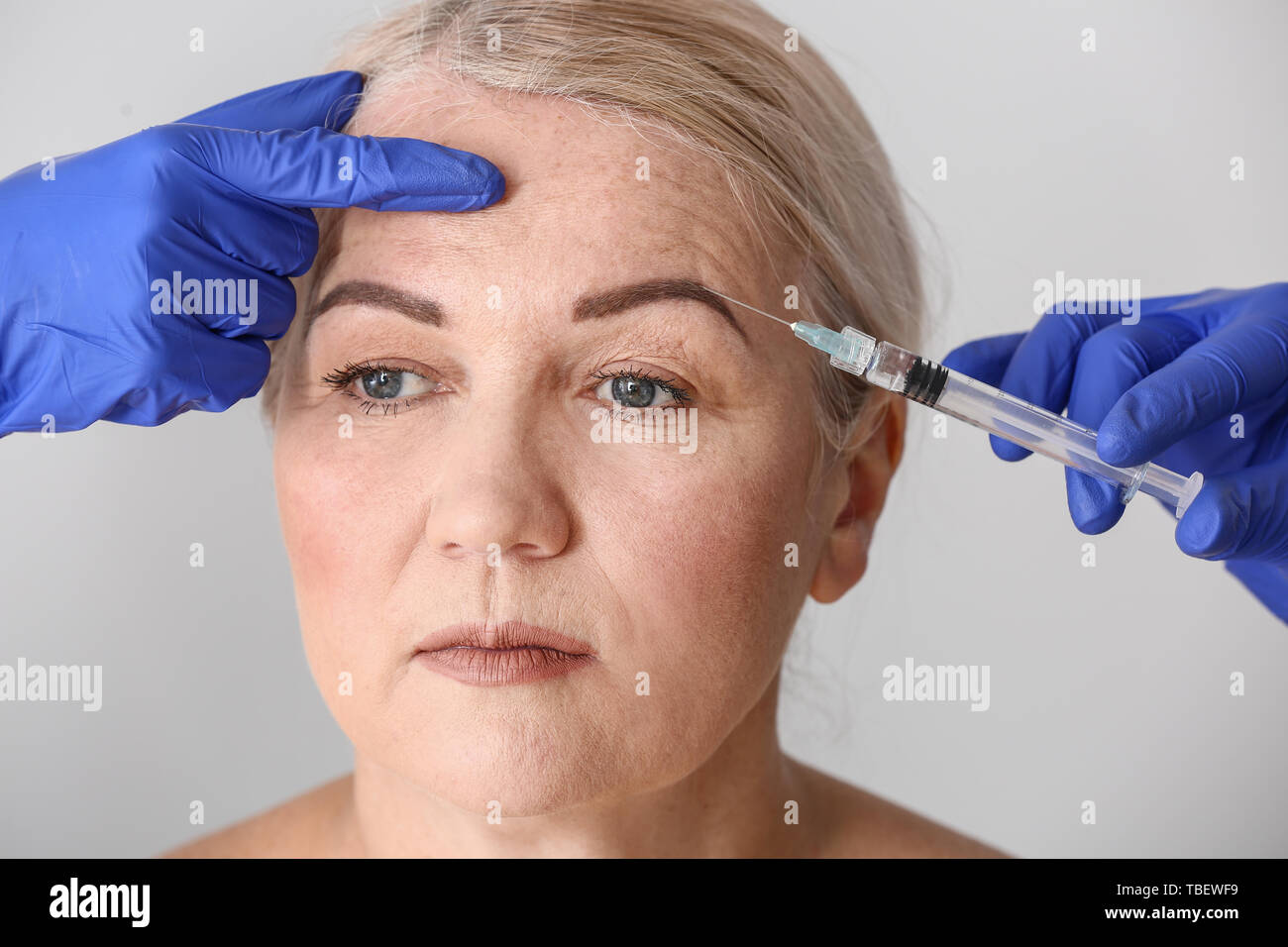 Mature woman receiving injection in face on light background Stock ...