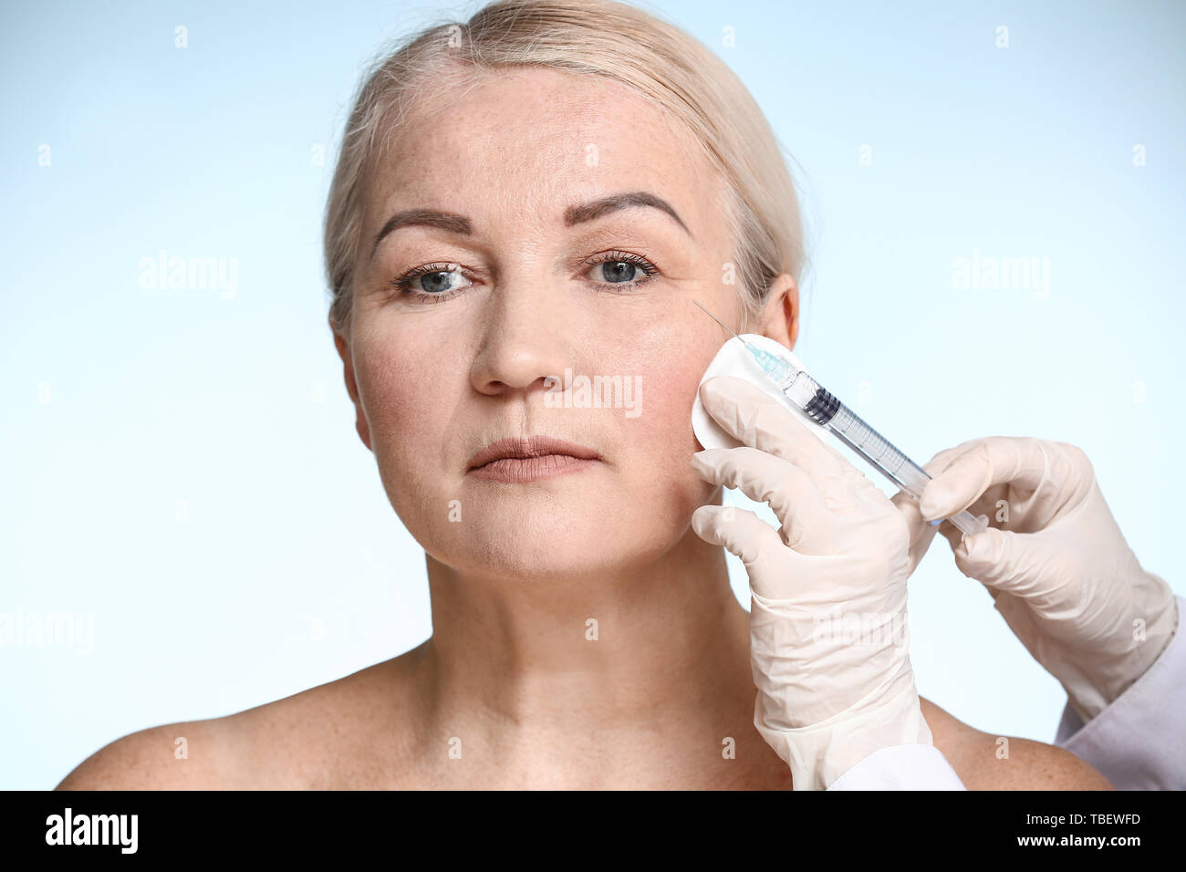 Mature woman receiving injection in face on color background Stock ...
