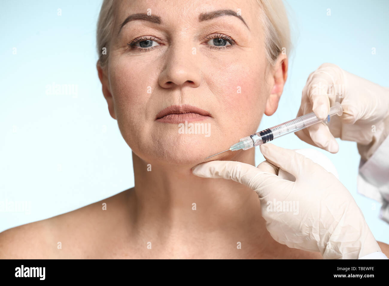 Mature woman receiving injection in face on color background Stock ...