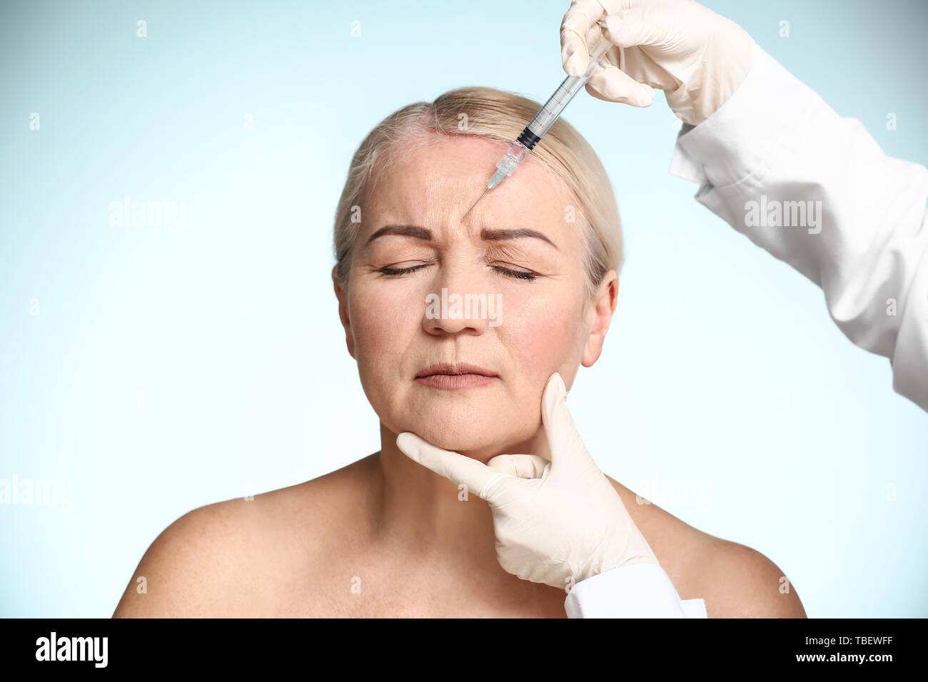 Mature woman receiving injection in face on color background Stock ...