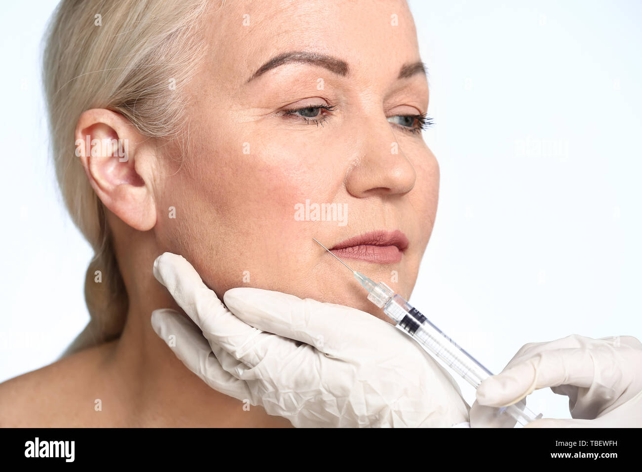 Mature woman receiving injection in face on color background Stock ...