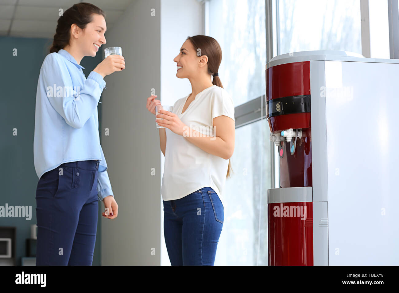 Colleagues drinking water from cooler during break in office Stock ...