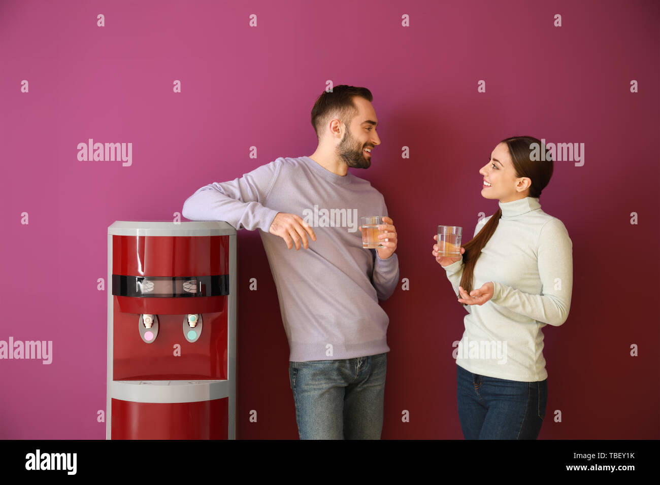 Man and woman drinking water from cooler against color background Stock ...