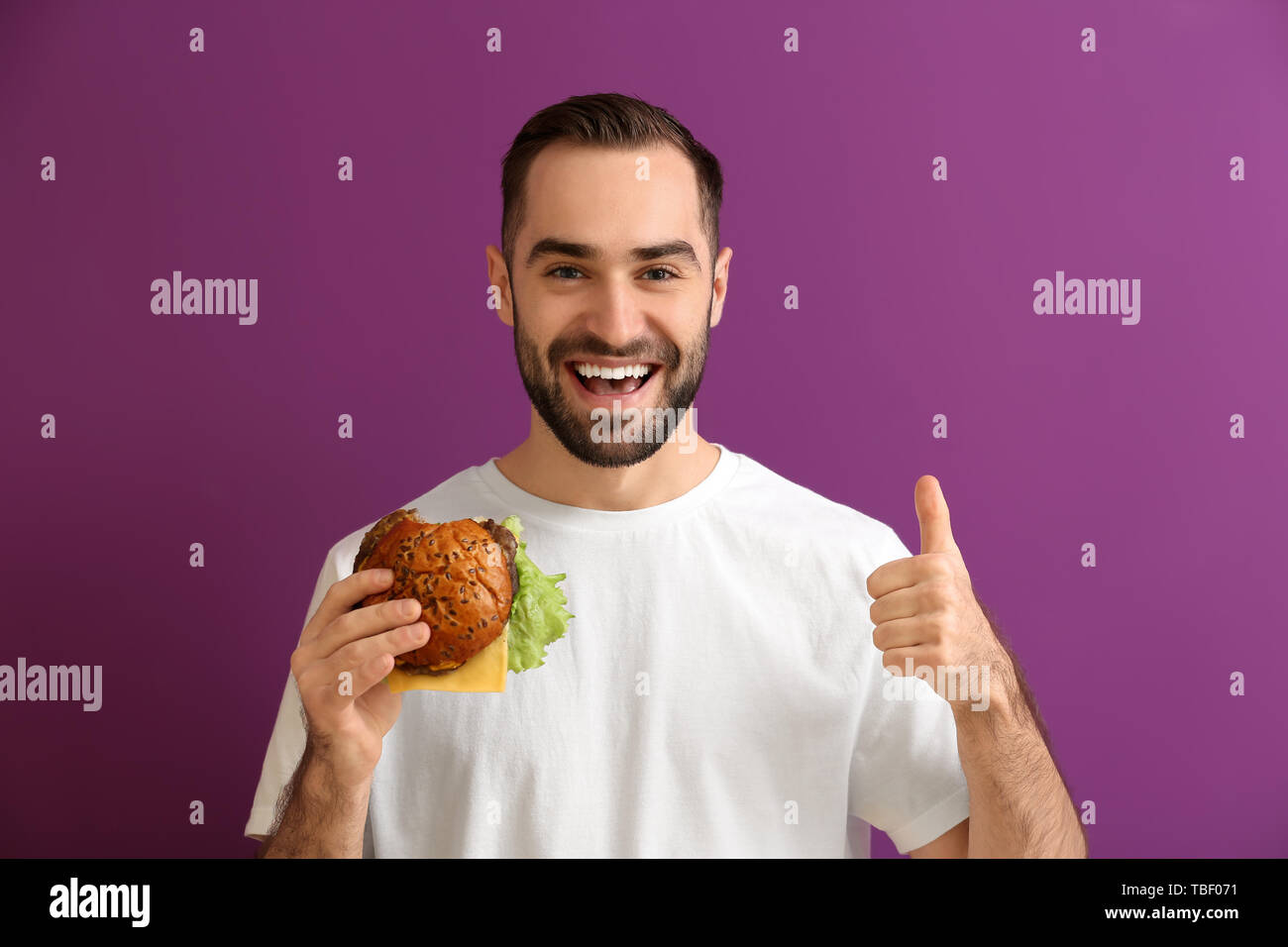 Man with tasty burger showing thumb-up on color background Stock Photo ...