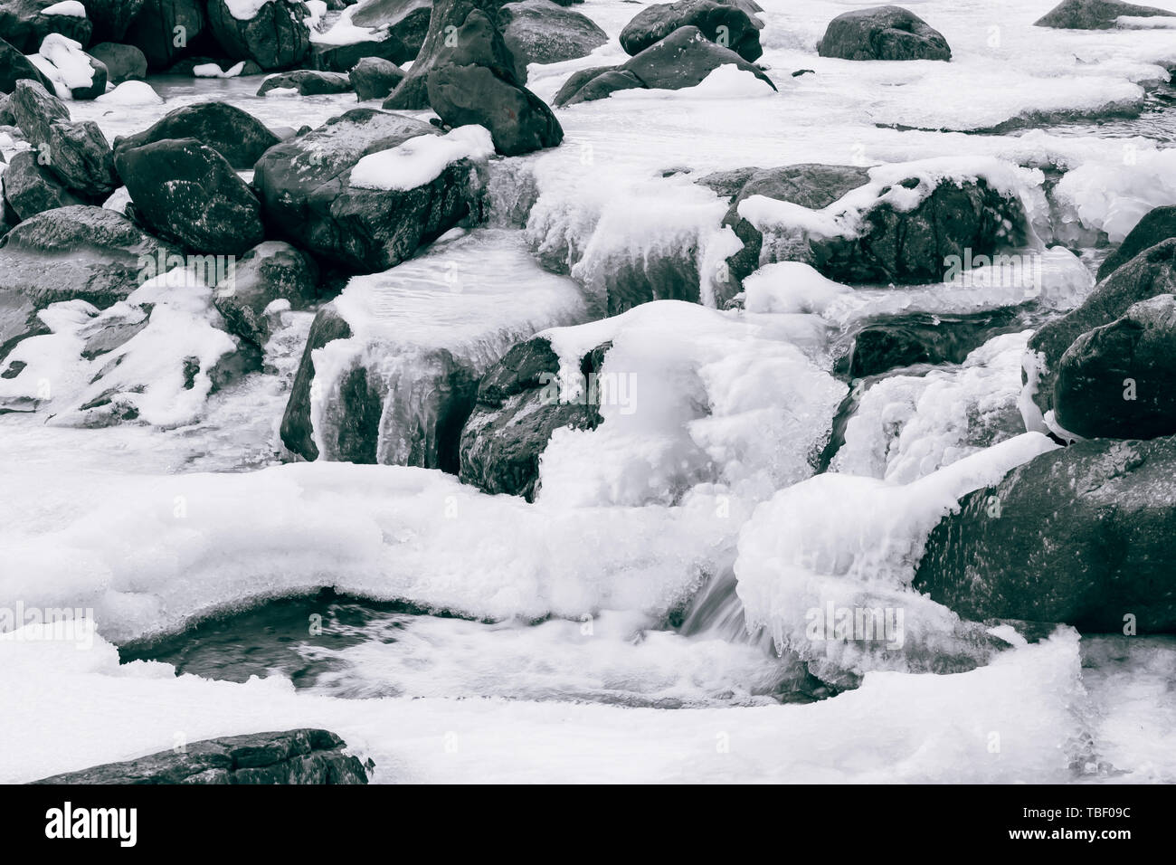 Winter mountain river under ice. Water froze and turned into icicles ...