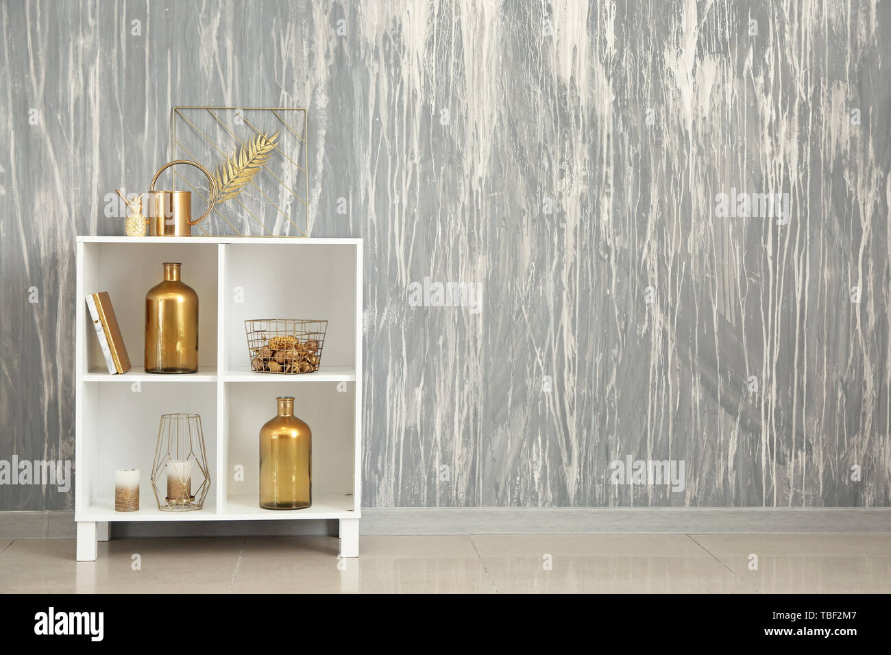 Rack with golden decor near grey wall in room Stock Photo - Alamy