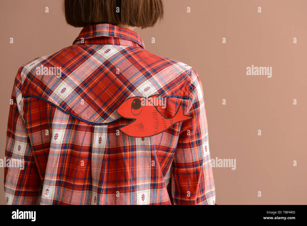 Paper fish on back of young woman against color background. April Fool ...