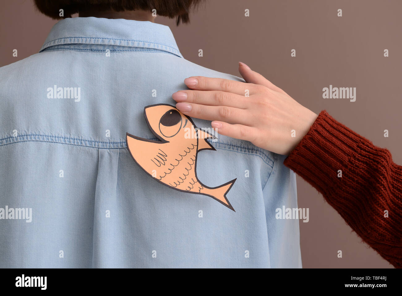 Woman sticking paper fish to her friend's back on color background ...