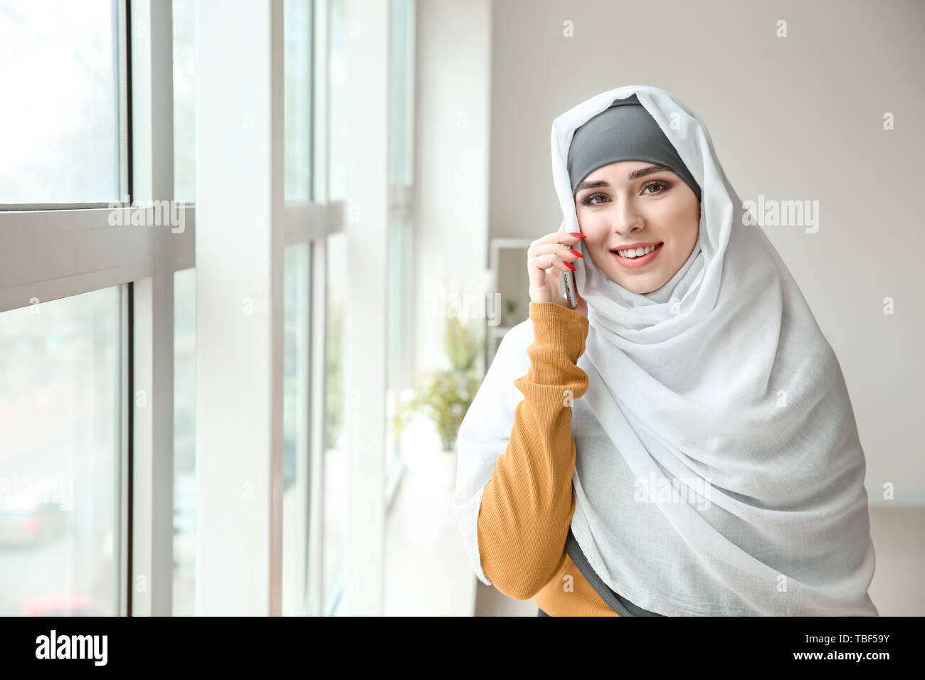 Beautiful Muslim woman talking by phone near window Stock Photo - Alamy