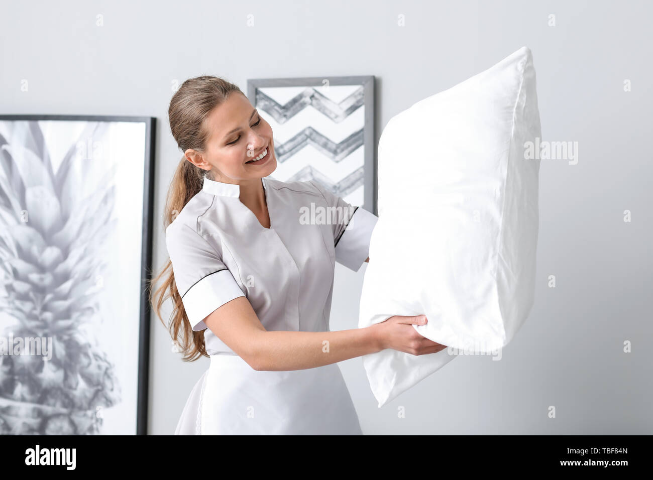 Beautiful female housekeeper with soft pillow in room Stock Photo - Alamy