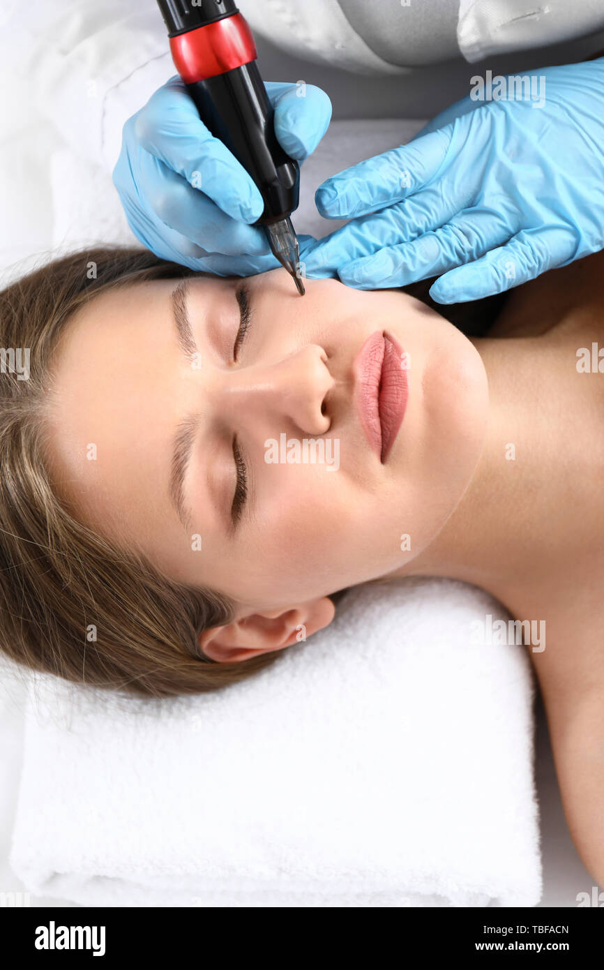 Young woman undergoing procedure of permanent makeup in beauty salon ...