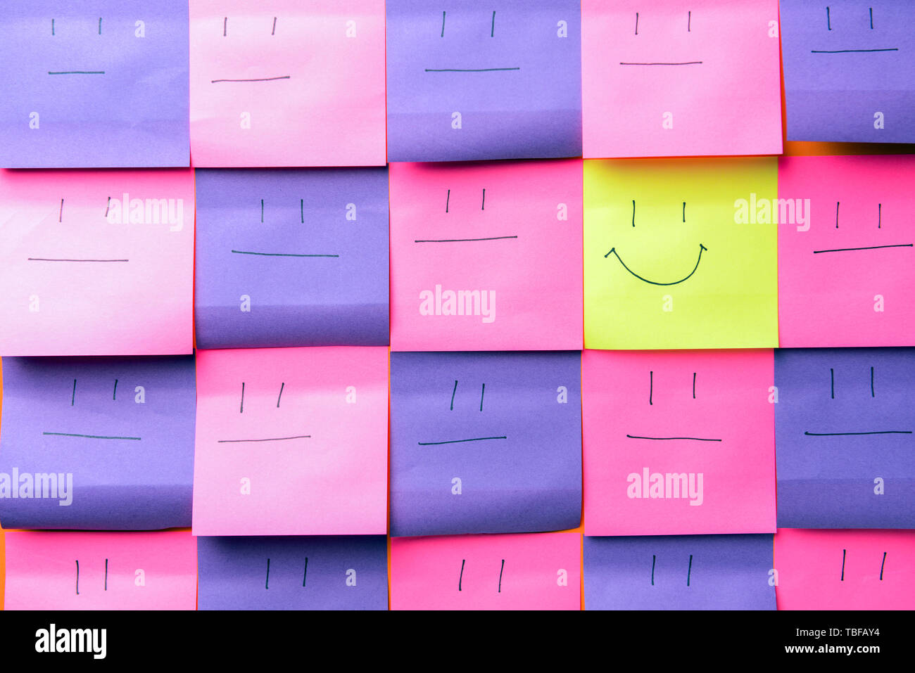 Paper sheet with drawn smiley emoticon among those with serious ones ...