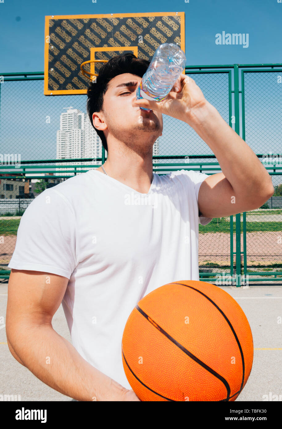 A strong cacusan male is drinking water on the basketball court while ...