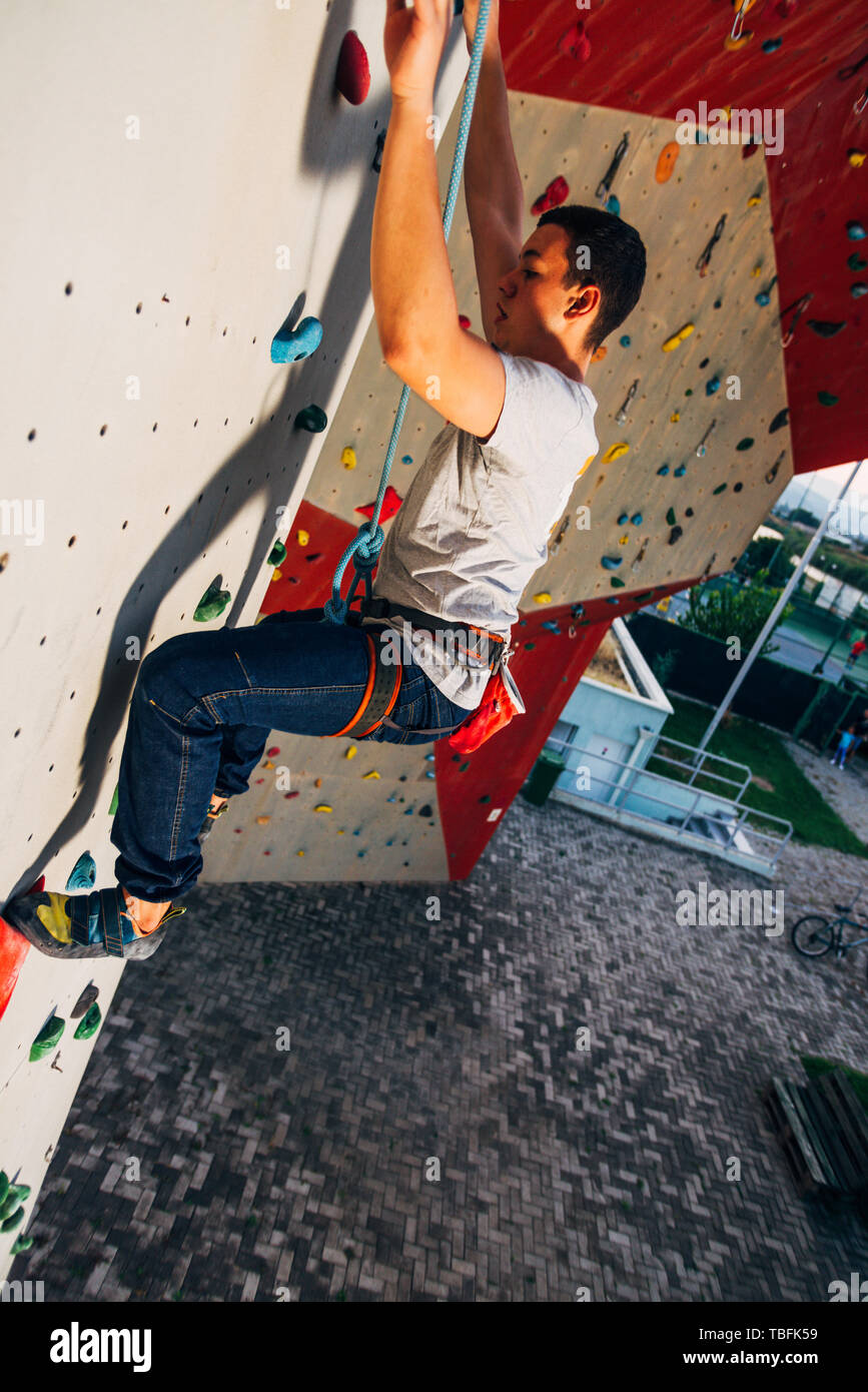 Man wearing belaying rope, climbing on a very high rock climbing wall ...