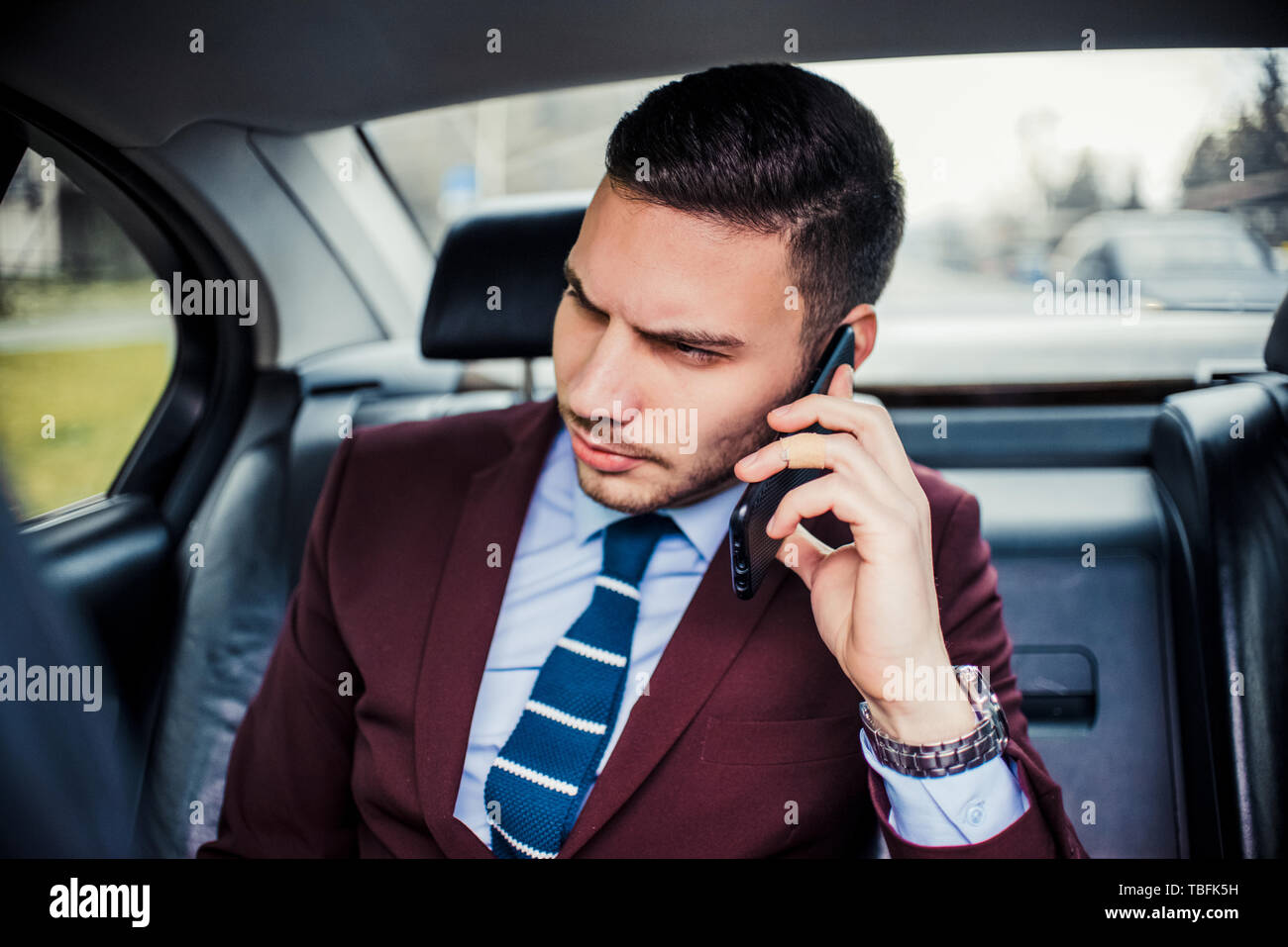 A good looking businessman is driving in a limo while talking on cell ...