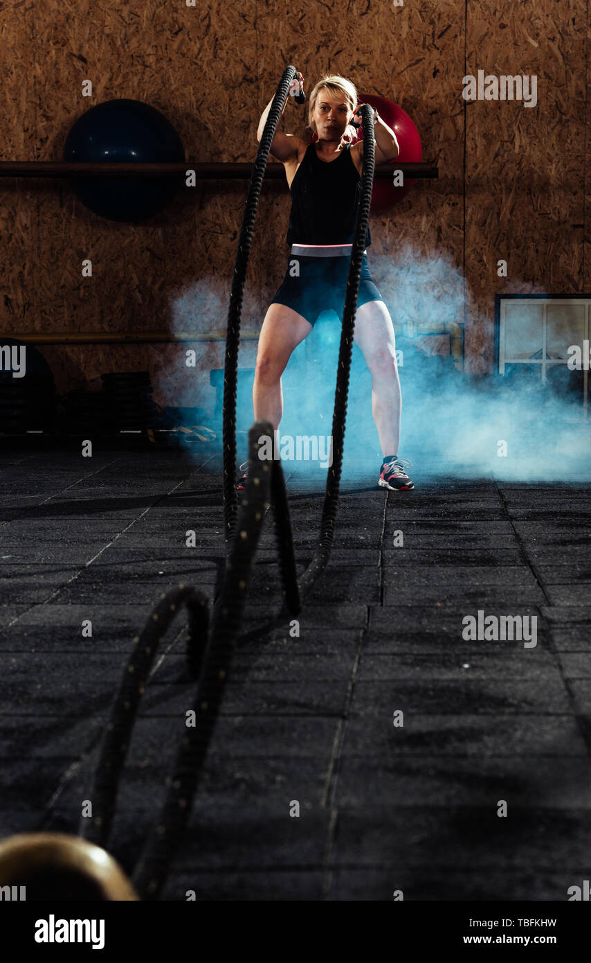 Female athlete making wave movement with battle rope during crossfit ...