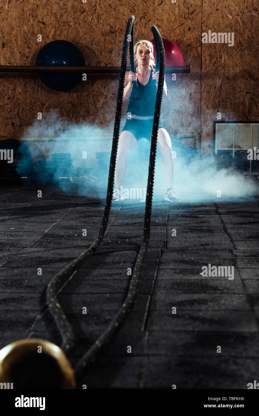 Athletic girl doing some cross-training exercises with a rope in gym ...