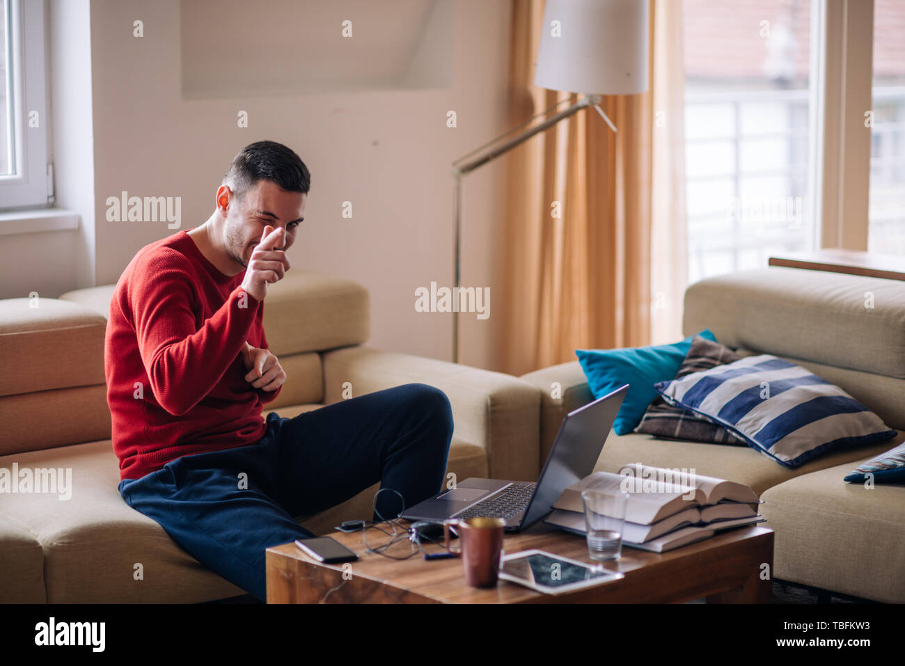 Tired student typing on his laptop and reading a book while sitting on ...