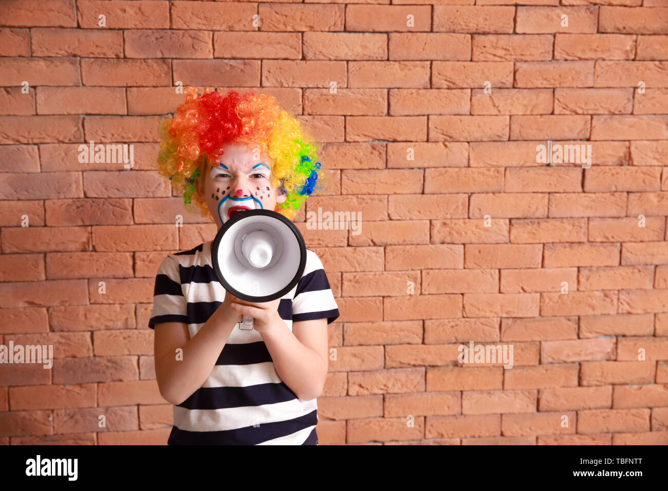 Cute little boy with clown makeup and megaphone against brick wall ...
