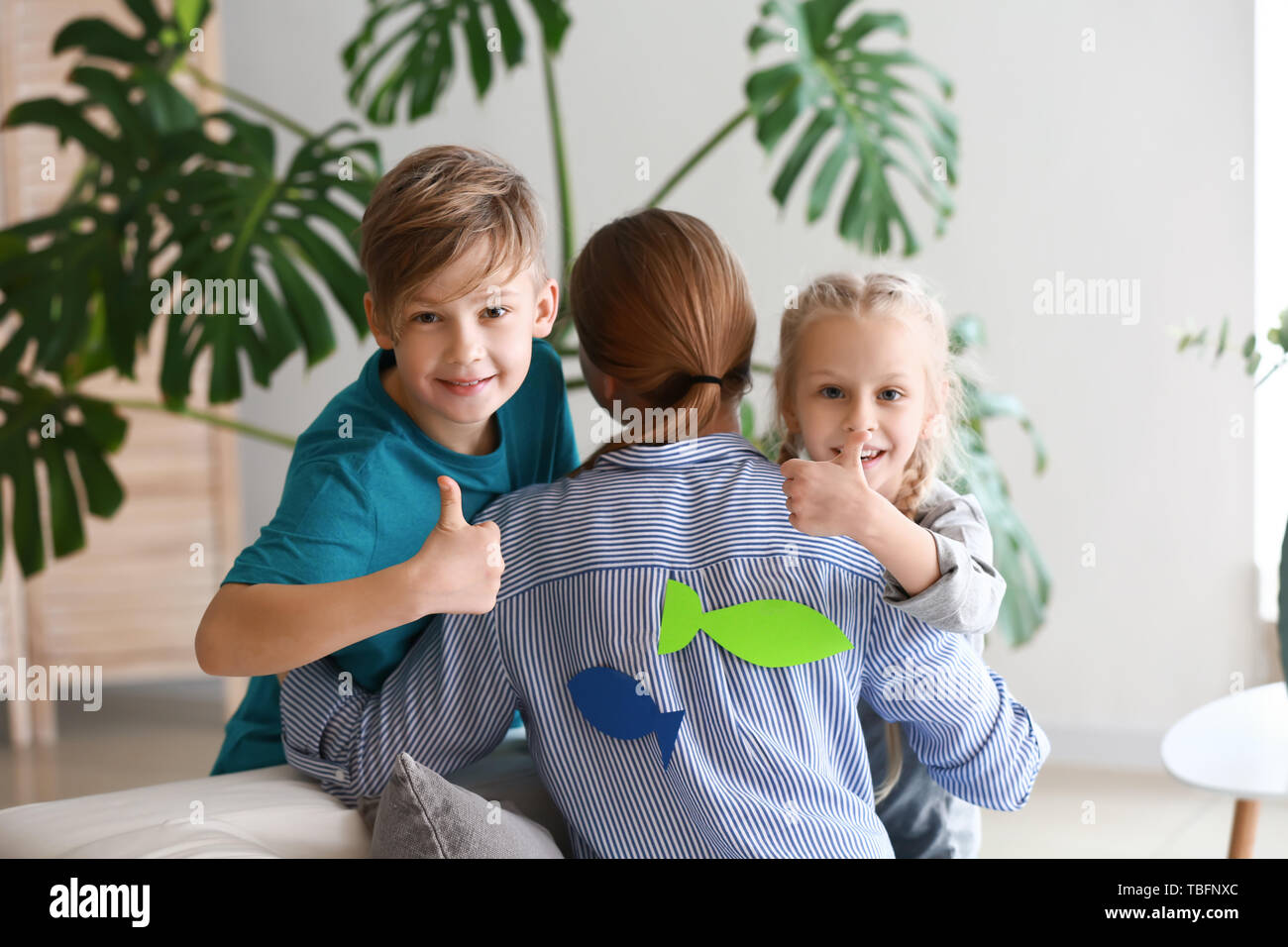 Little children sticking paper fish to their mother's back. April fools ...