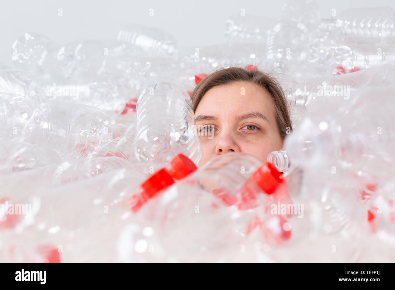 Dehydrated sick woman is lying in a pile of plastic bottles ...