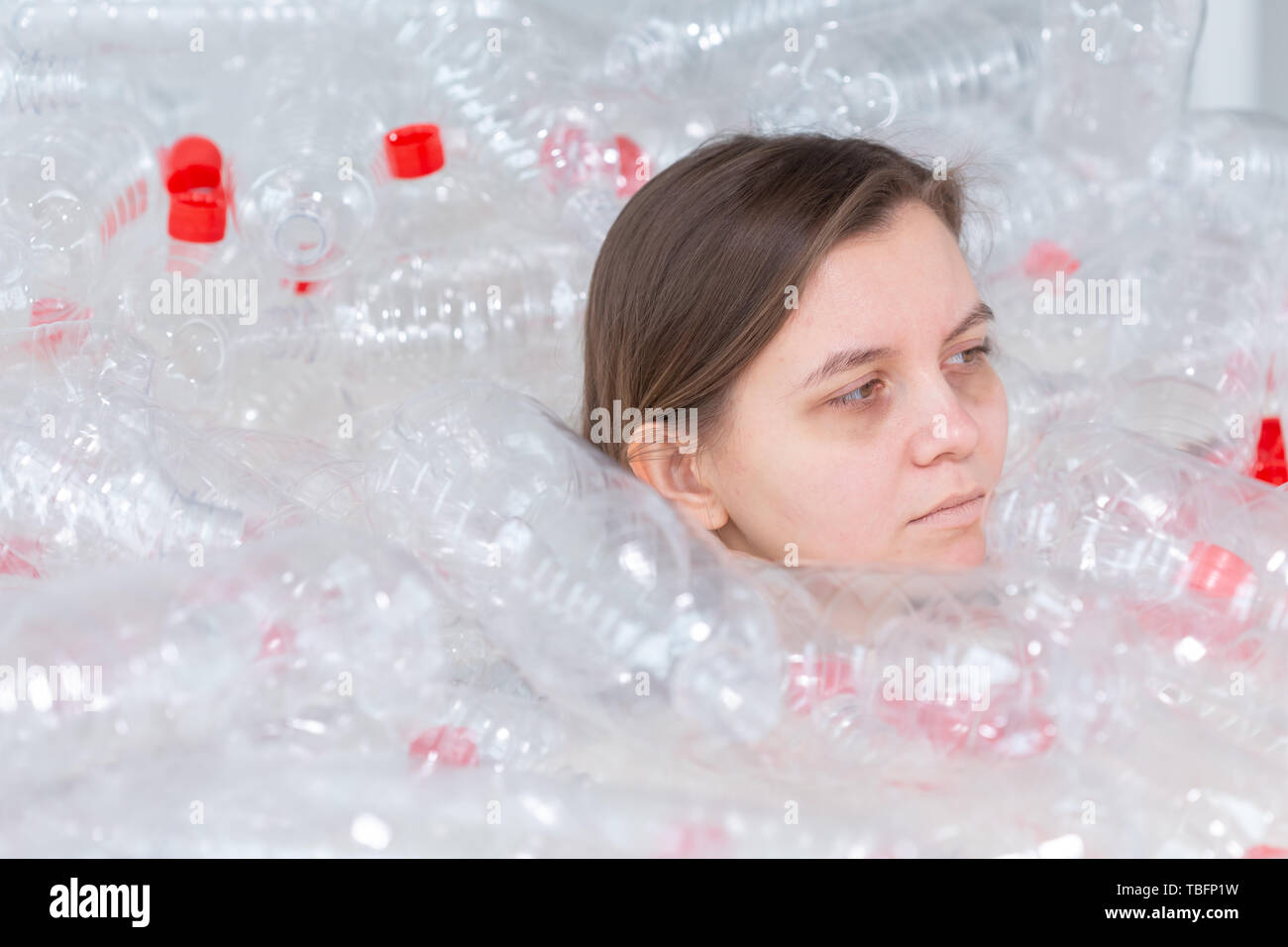 Dehydrated sick woman is lying in a pile of plastic bottles ...