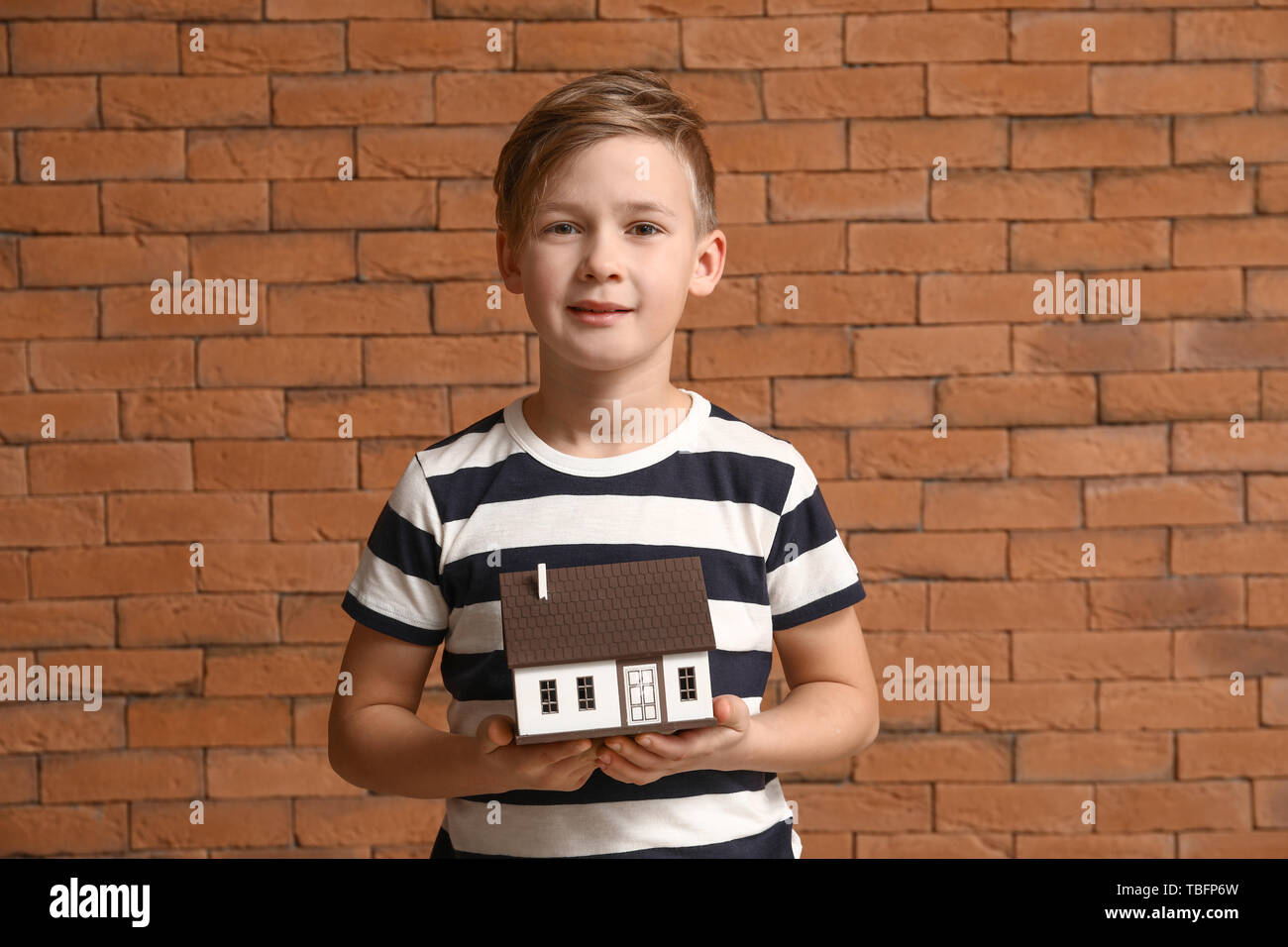 Little boy with model of house on brick background. Concept of ...