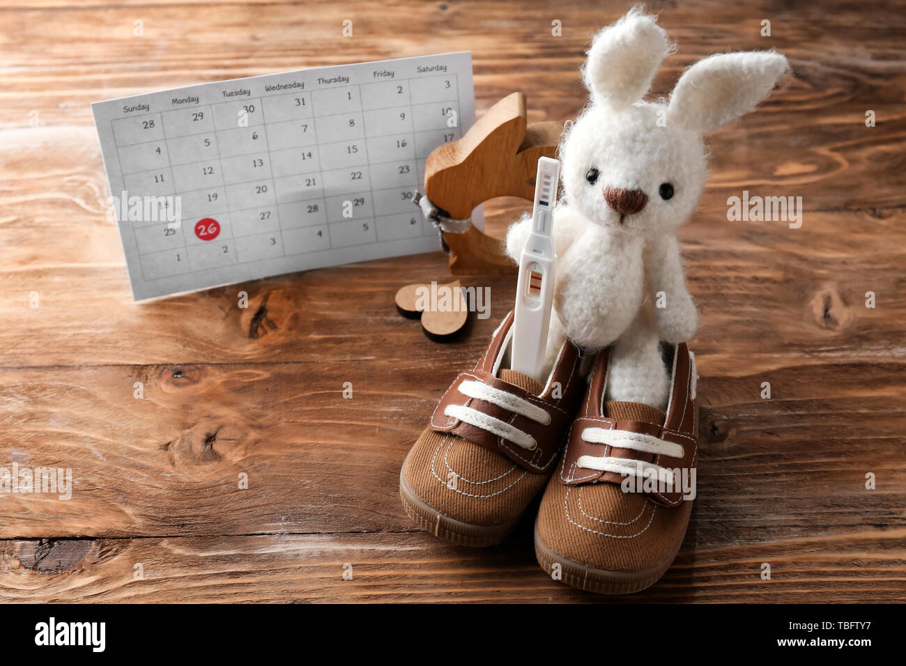 Baby booties, toy rabbit, pregnancy test and calendar on wooden ...