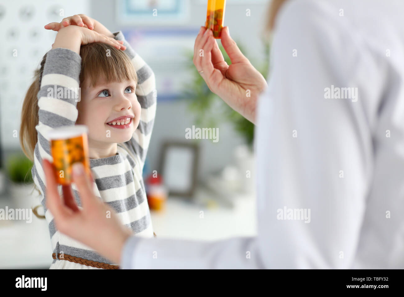 Cute little patient girl having fun selecting a bottle of medications ...