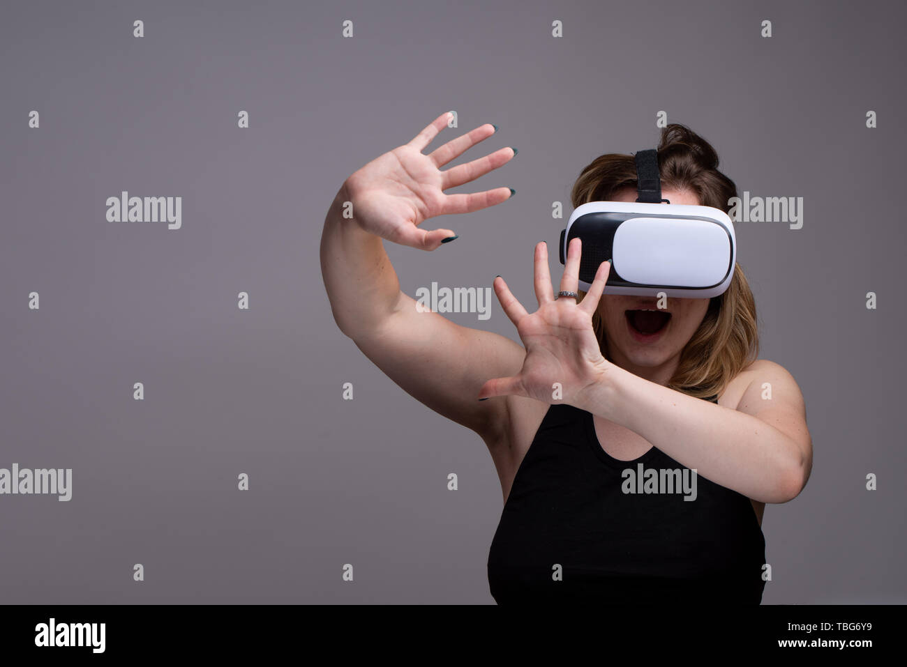 Young female using 3D VR gadget is displaying a terrified and shocked ...