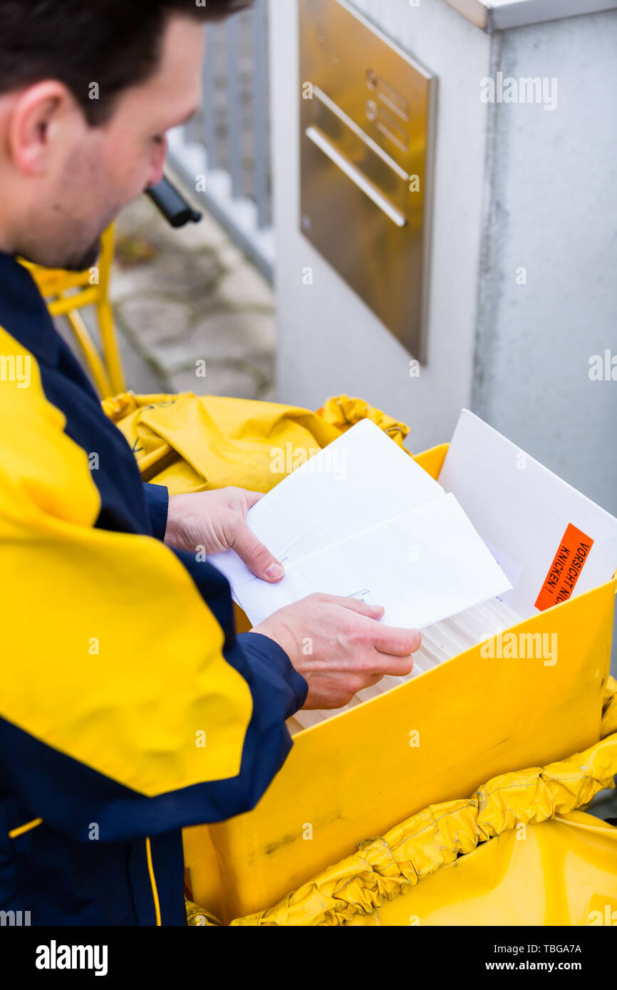 Postman delivering letters to mailbox of recipient Stock Photo - Alamy