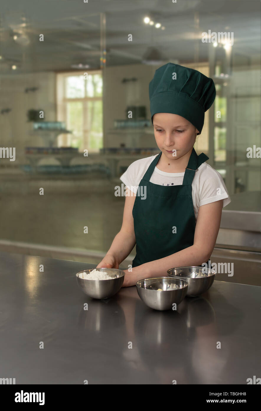 Beautiful young cook chef girl in green chef cap mixes the ingredients ...
