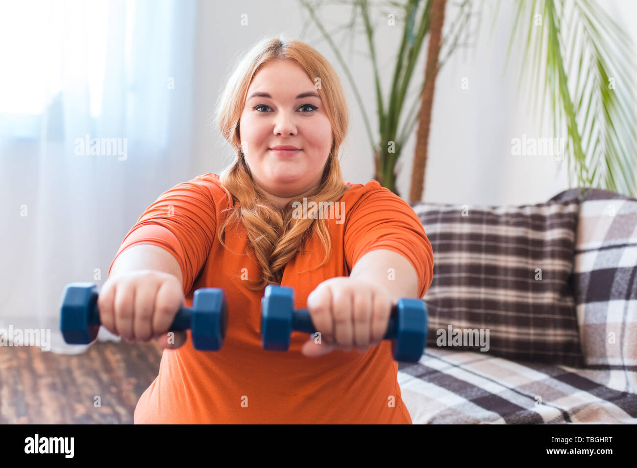 Chubby woman sport at home sitting on stability ball holding dumbbells ...