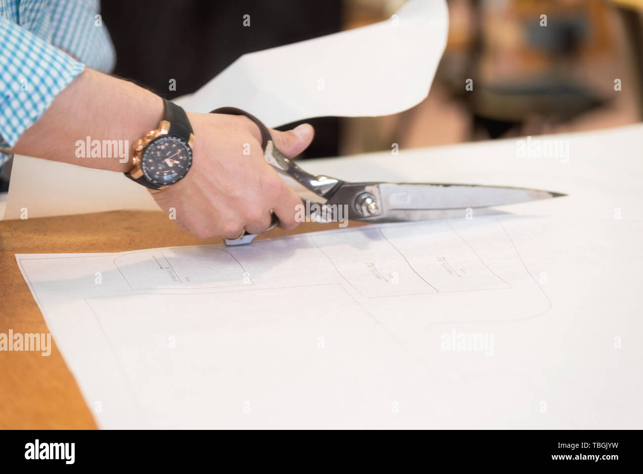 Tailor cutting out the marked pattern on fabric with large scissors on ...