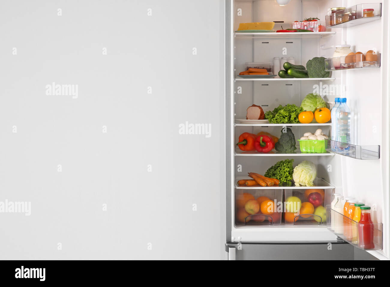 Open fridge full of food near white wall Stock Photo - Alamy