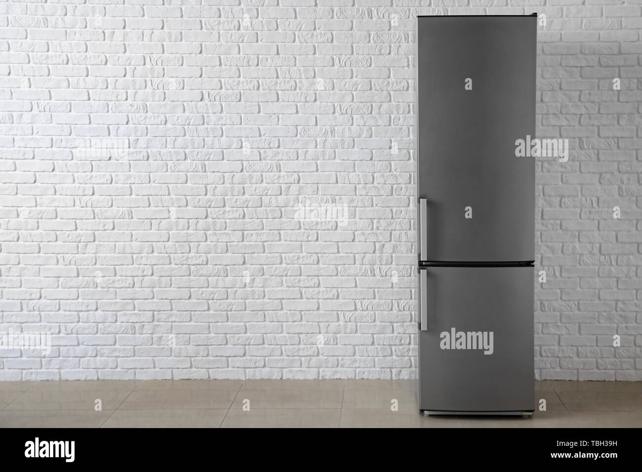 Modern fridge near white brick wall Stock Photo - Alamy
