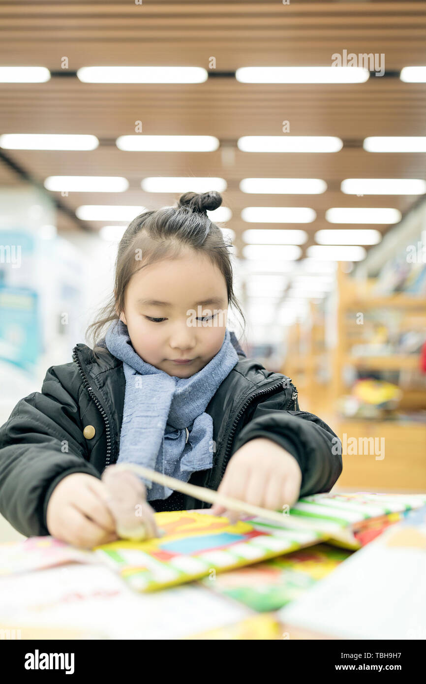 Little Asian girl reading in the library Stock Photo - Alamy