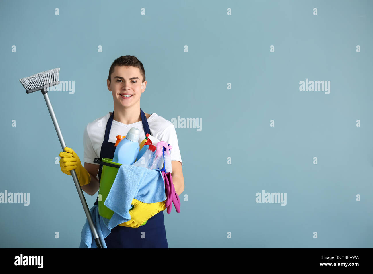 Portrait of male janitor with cleaning supplies on grey background ...