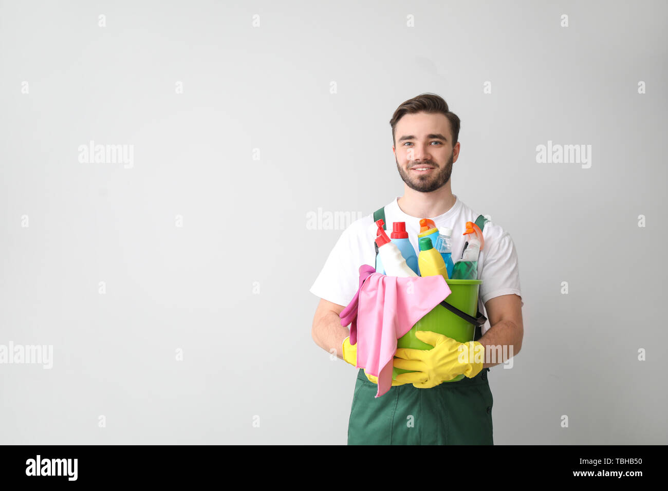 Portrait of male janitor with cleaning supplies on light background ...