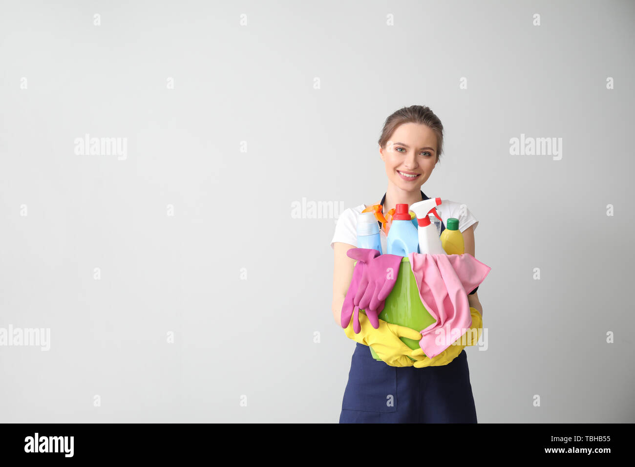 Portrait of female janitor with cleaning supplies on light background ...