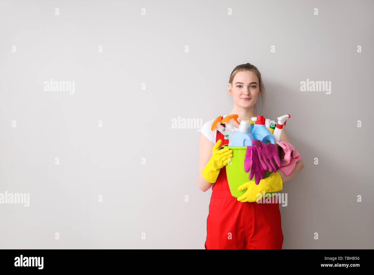 Portrait of female janitor with cleaning supplies on light background ...
