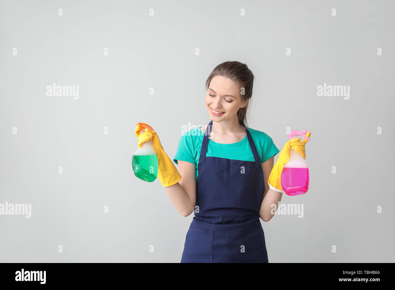 Portrait of female janitor with bottles of detergent on light ...