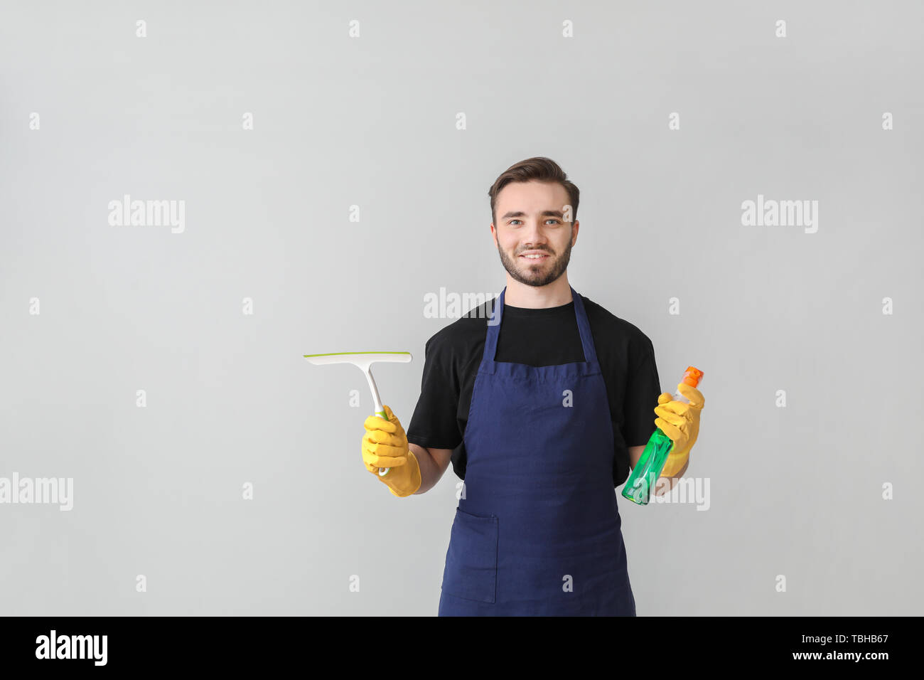 Portrait of male janitor with cleaning supplies on light background ...