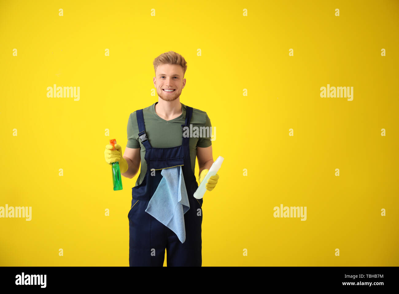 Portrait of male janitor with cleaning supplies on color background ...