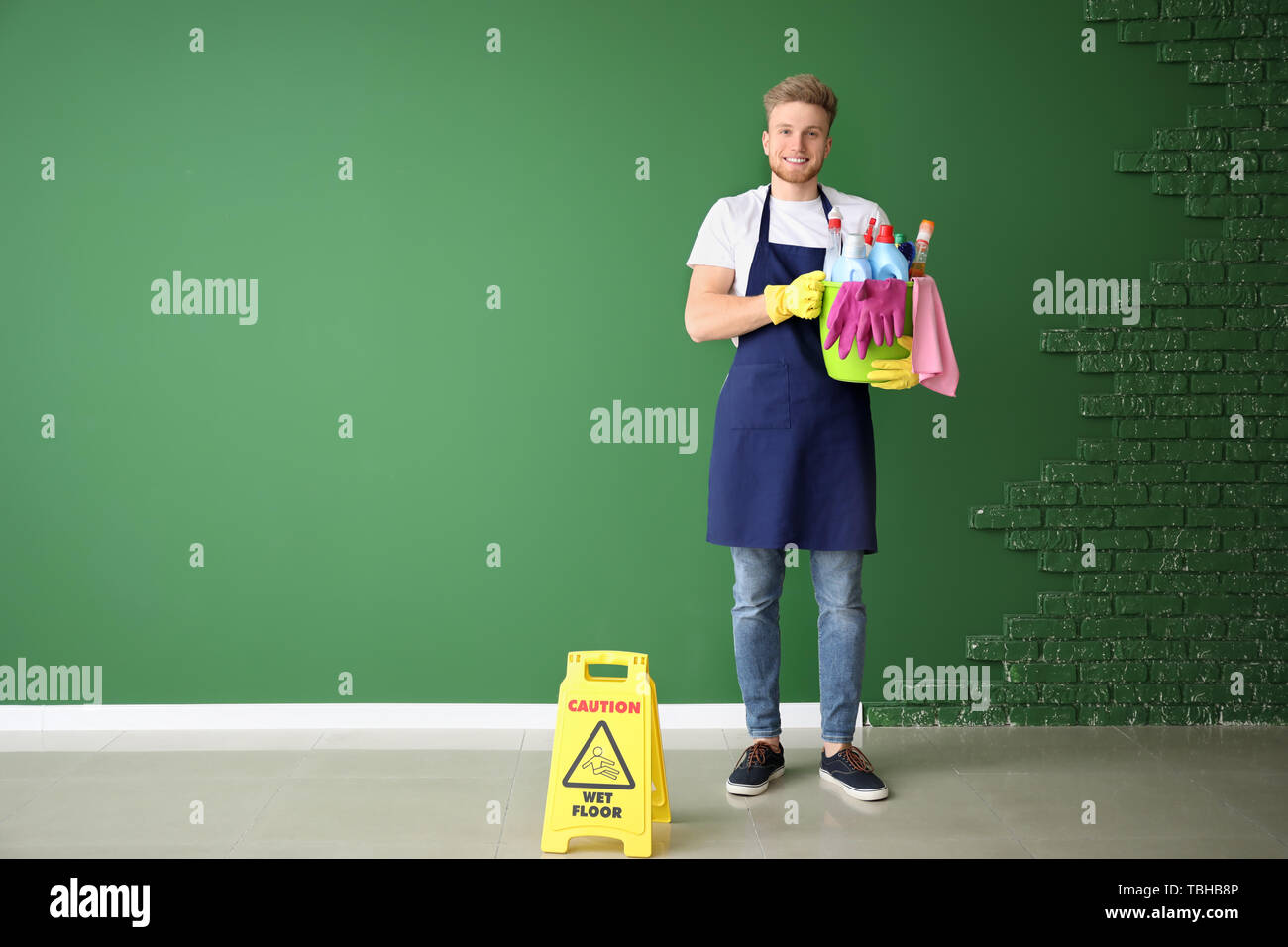 Male janitor with cleaning supplies near color wall Stock Photo - Alamy