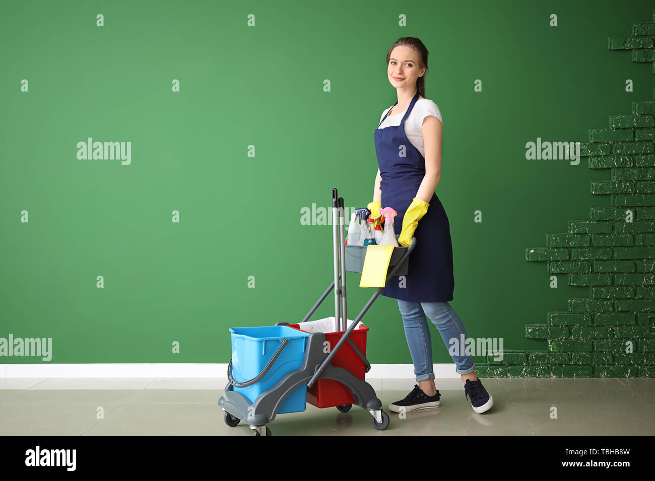 Female janitor with trolley near color wall Stock Photo - Alamy