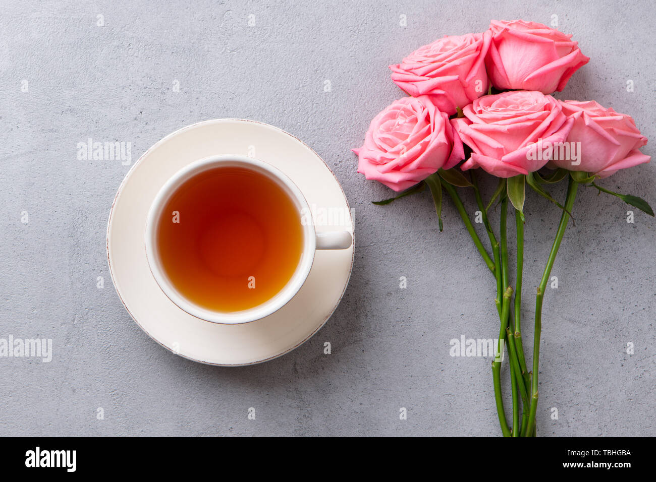 Cup of tea with pink rose. Top view. Copy space. Grey stone background ...