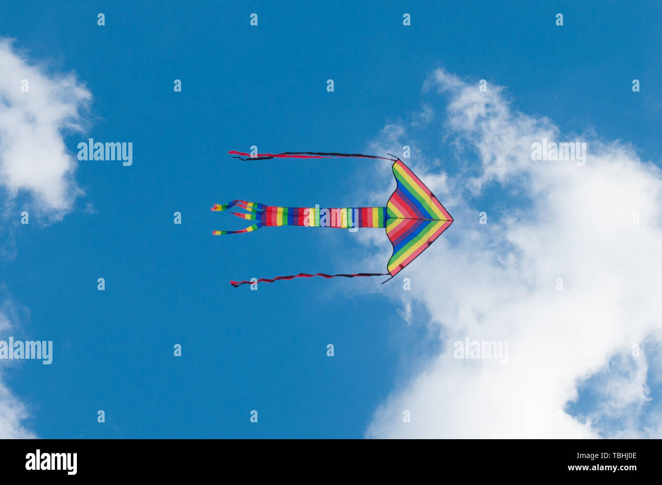 Fun rainbow coloured Kite on a blue sky in the shape of an arrow. Can ...